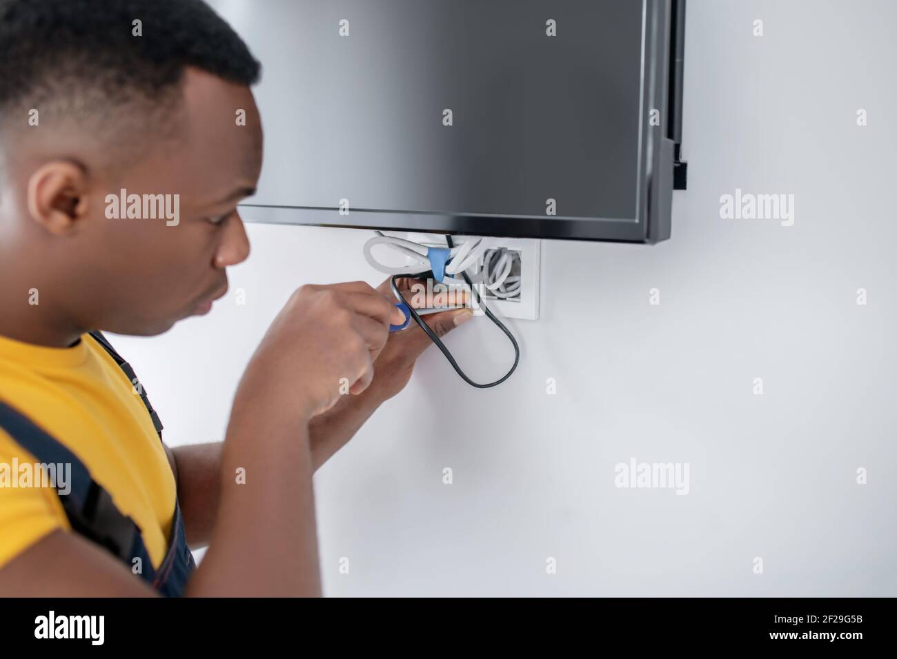 Dark-skinned service man in yellow tshirt installing a tv Stock Photo ...