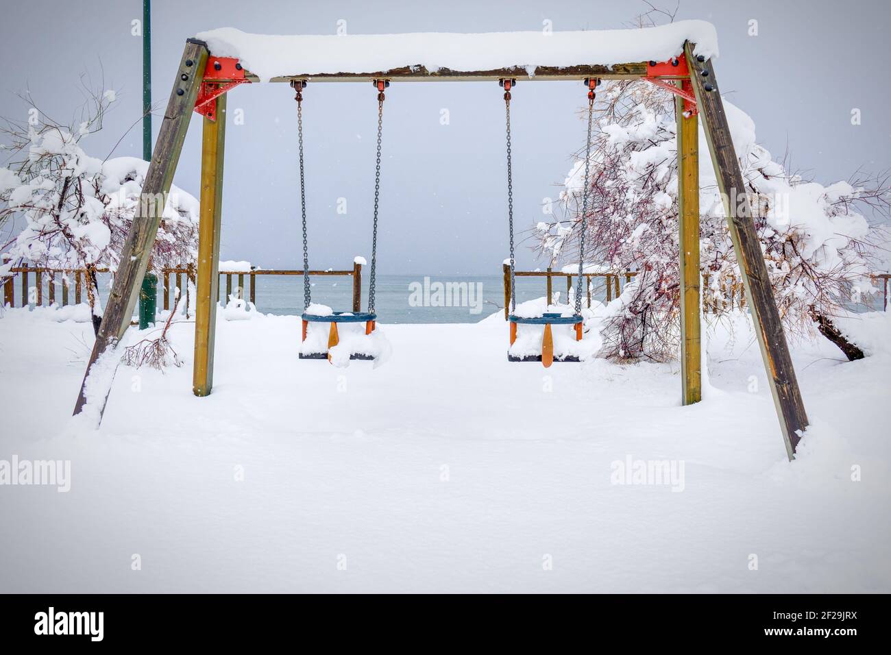 Snowy swings on playground with sea background Stock Photo - Alamy