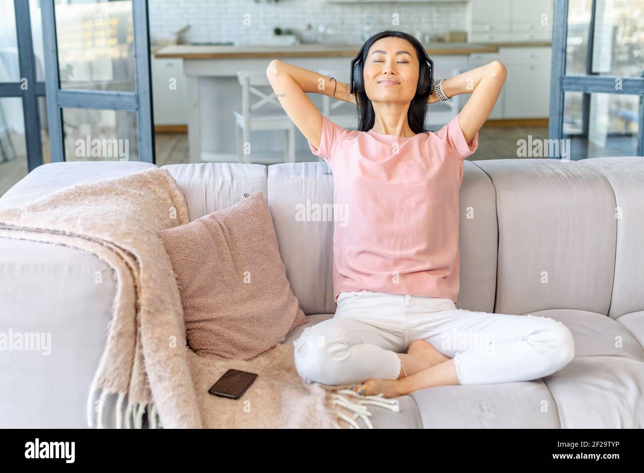 Young adult Asian woman in wireless headphones and stretchable clothes ...