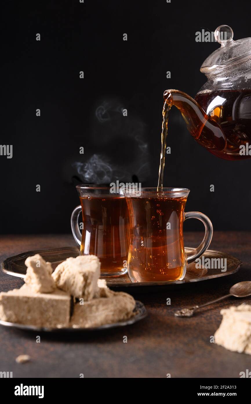 Pouring hot tea to special glass cups. Tea ceremony with halva on dark ...