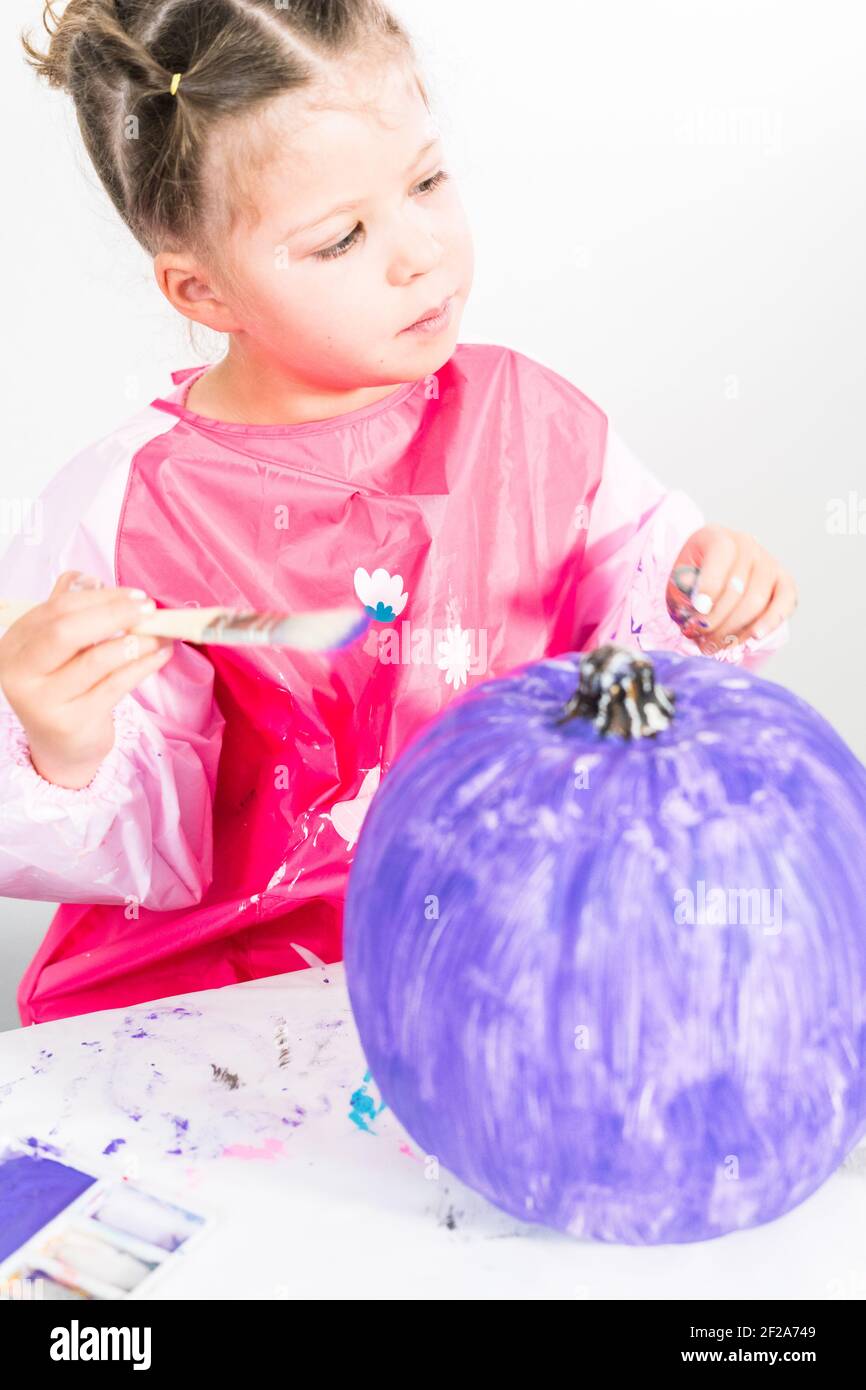 Little girl painting small craft pumpkin with purple acrylic paint ...