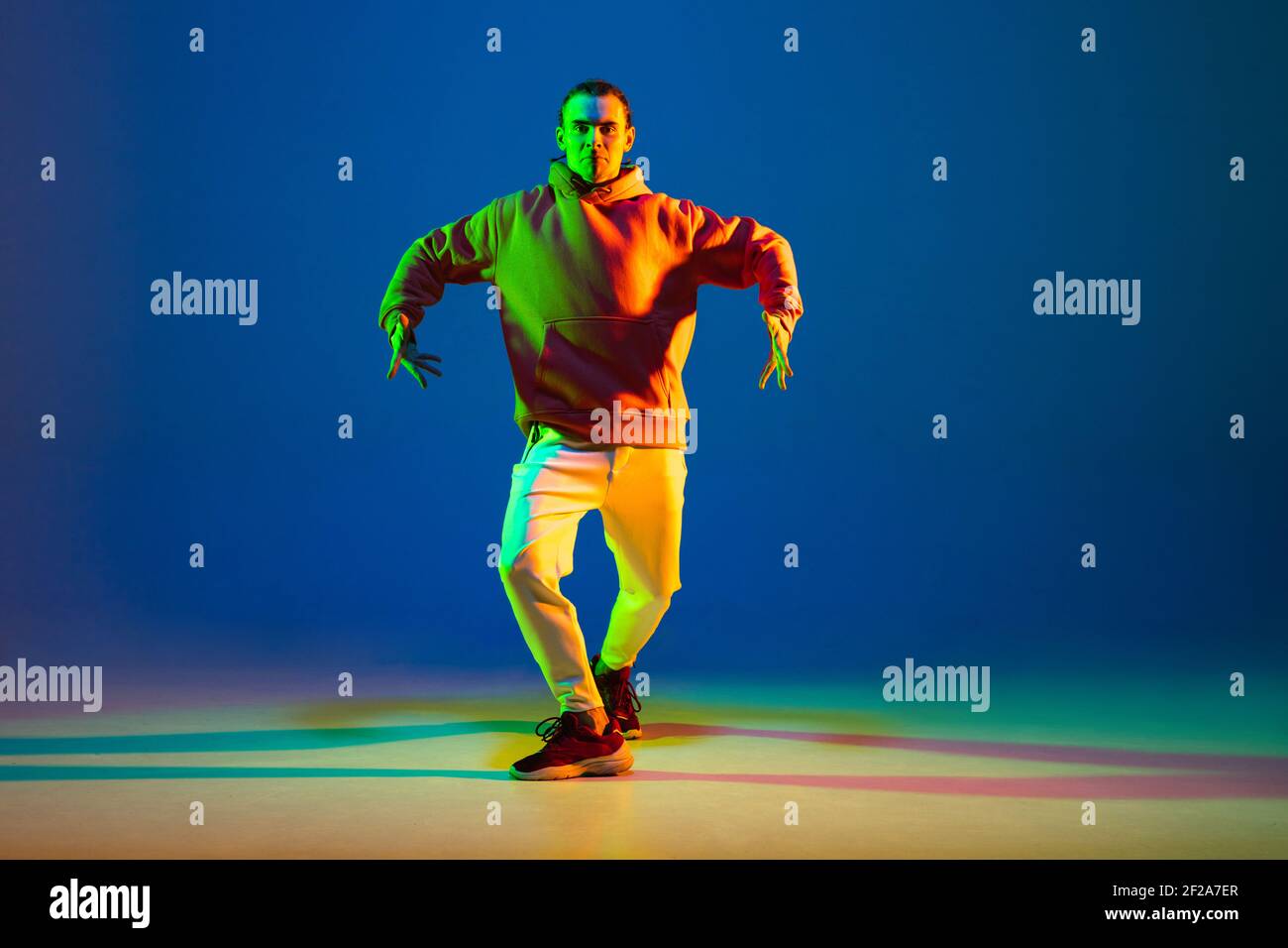 Young hip-hop dancer dancing isolated over blue background in neon ...