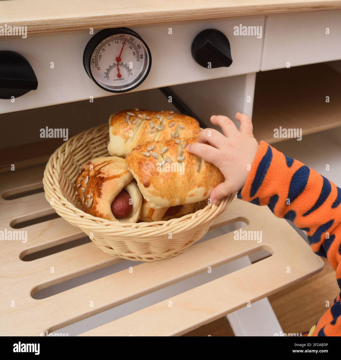 Unhealthy baby food. Baby reaching for sausage bread roll in toy kithen ...