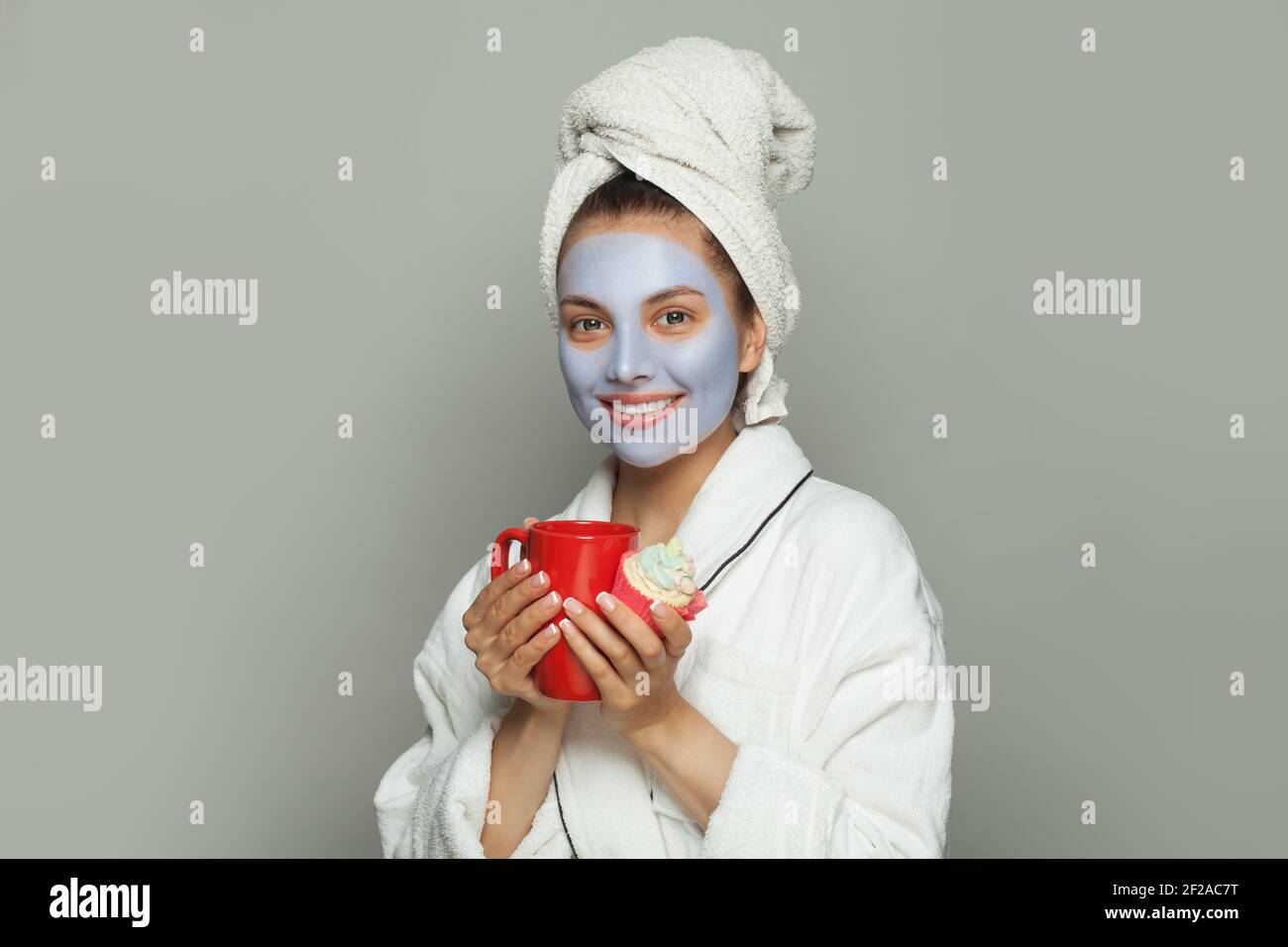 Young happy woman in cosmetic face mask eating breakfast and drinking ...