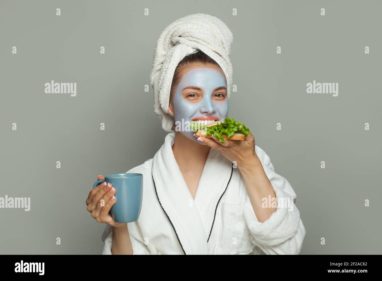 Pretty woman in cosmetic face mask eating breakfast and drinking coffee ...