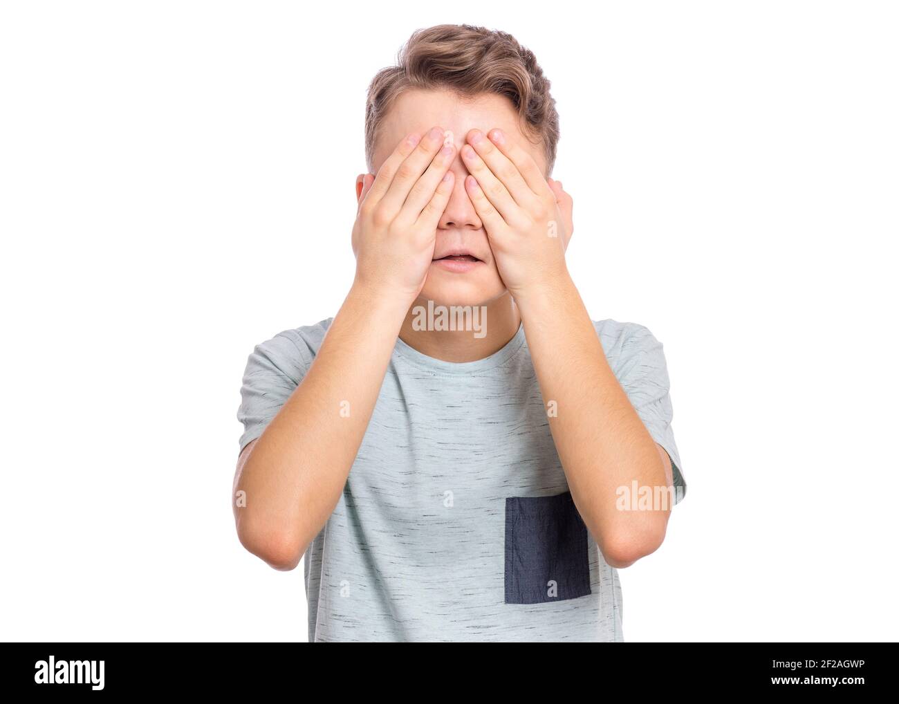 Handsome teen boy with sad expression covering face with hands while ...