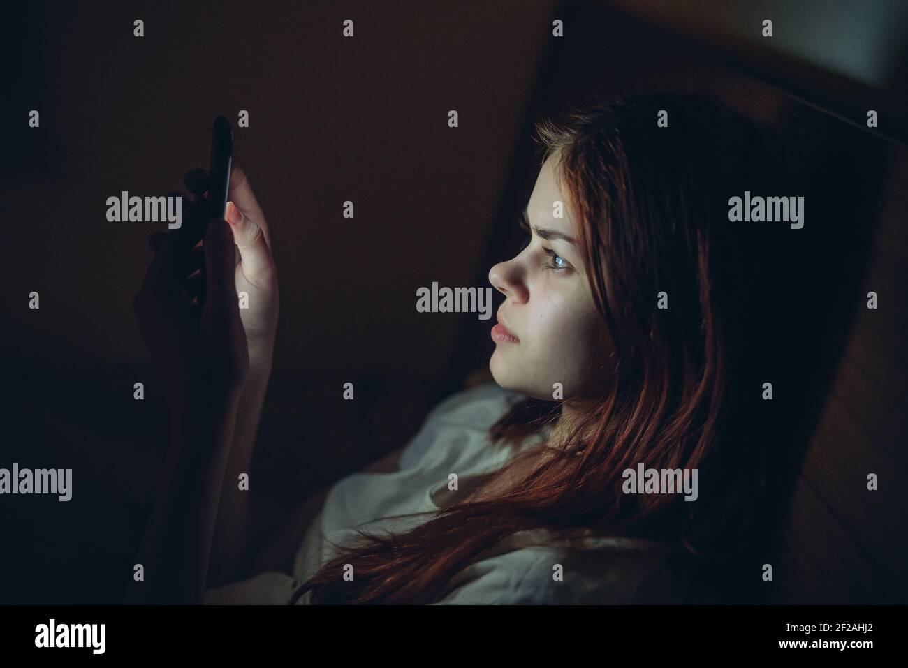 pretty woman lying in bed with phone in hand at night rest before ...