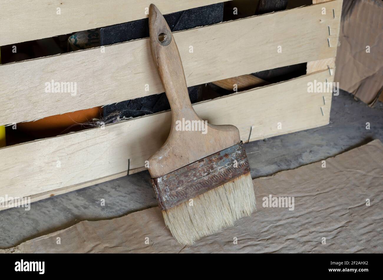 An old paintbrush stands by a wooden box. A wide brush with a wooden ...