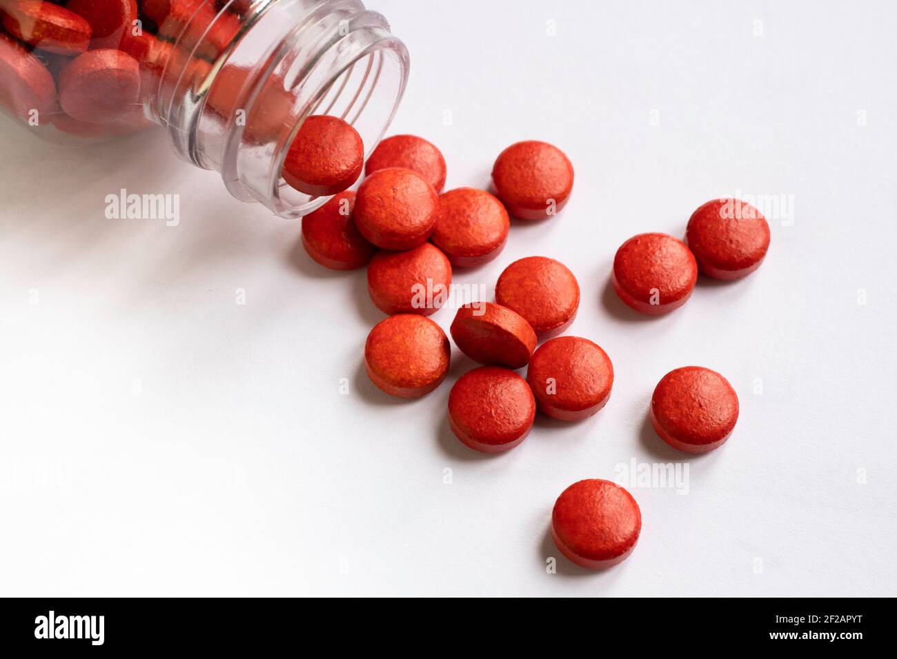 Red pills and tablets spilling out from glass pill bottle on white ...