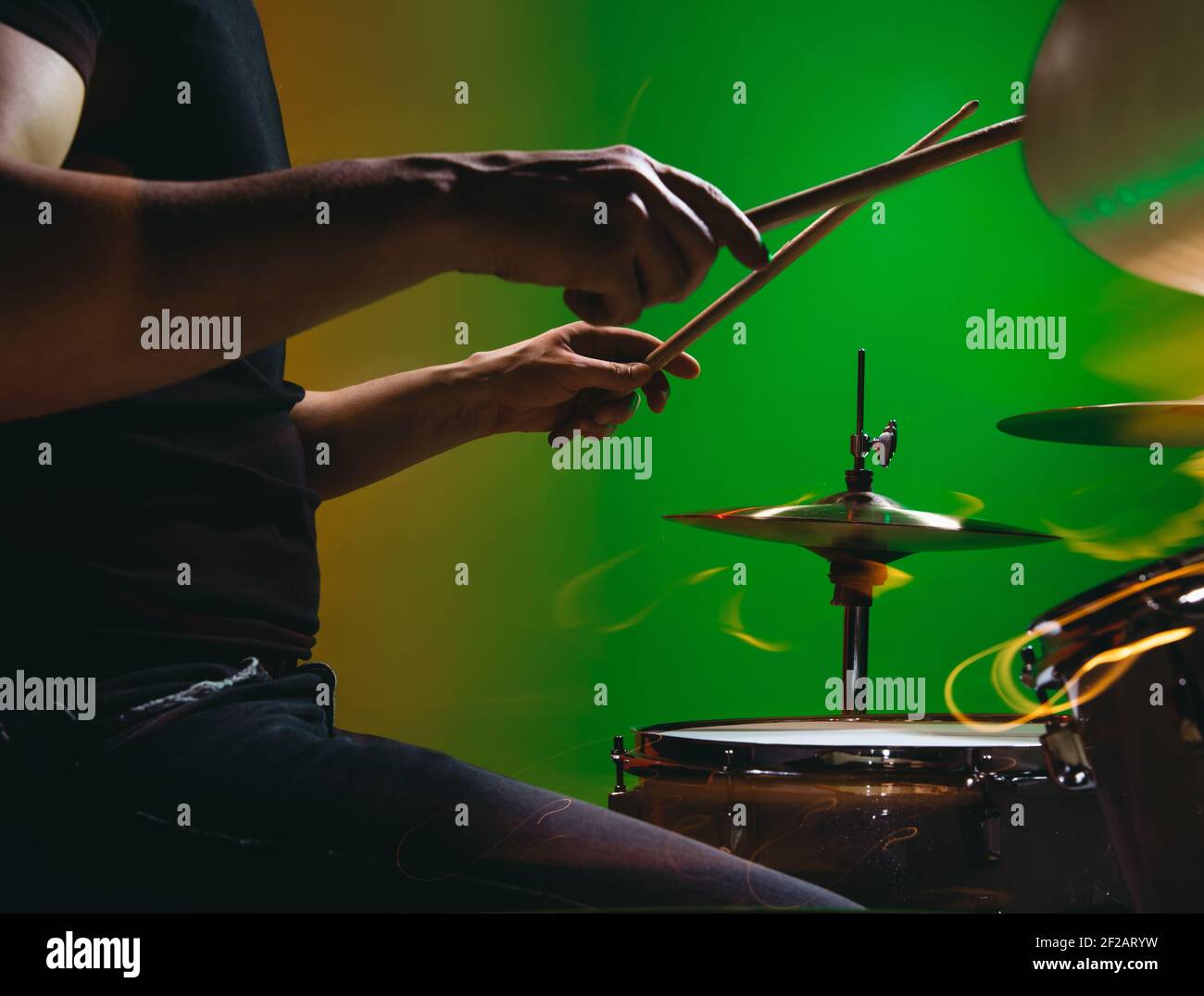 Close-up of male hands playing drums isolated on green-red background ...
