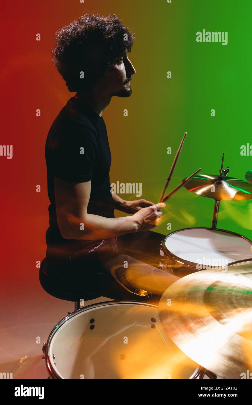 Portrait of young man drummer playing isolated on green-red background ...