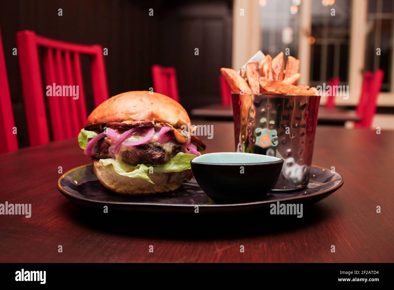 Juicy beef burger with red onion, french fries in a shiny metal bucket ...