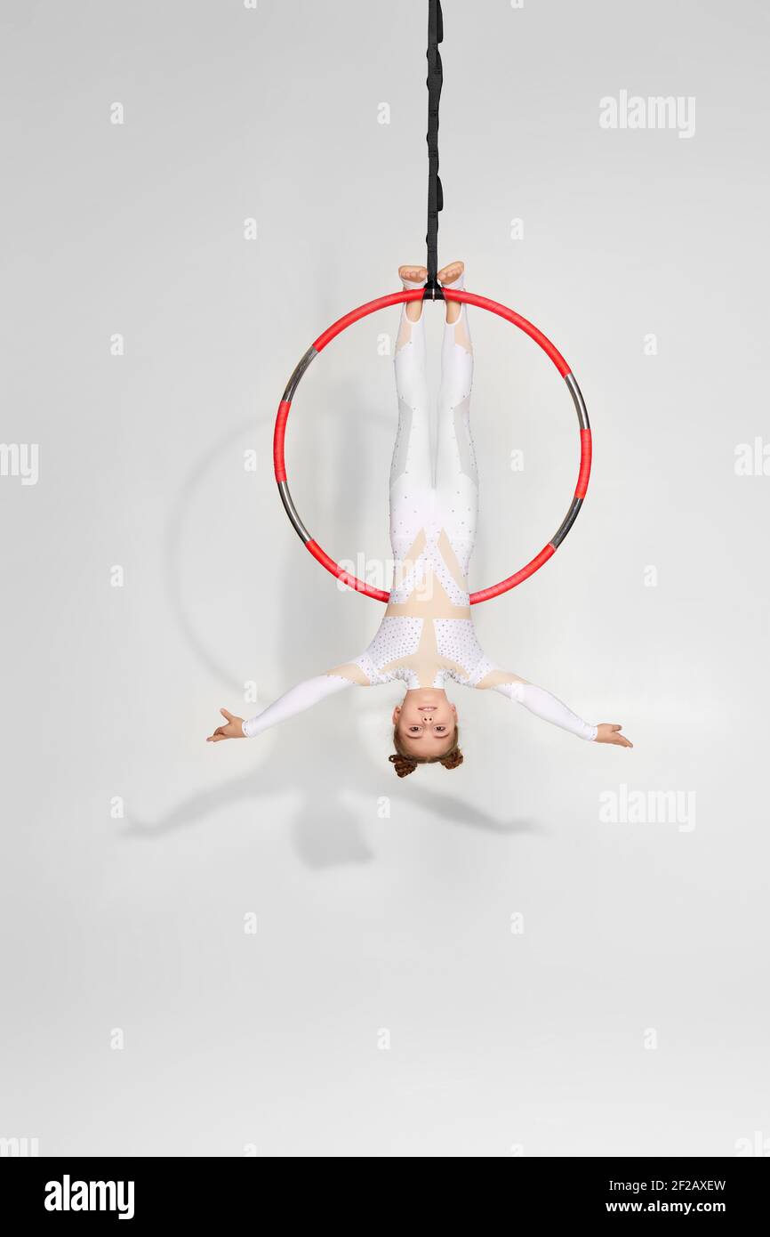 Little acrobat girl shows an acrobatic performance on an aerial hoop ...