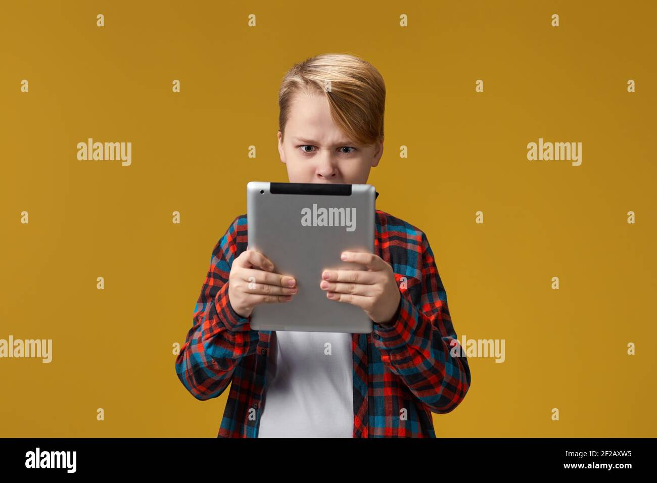angry child boy in checkered shirt using digital tablet on yellow ...
