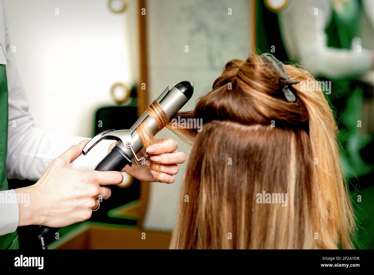 Back view of female hairdresser's hands curling women's hair with ...