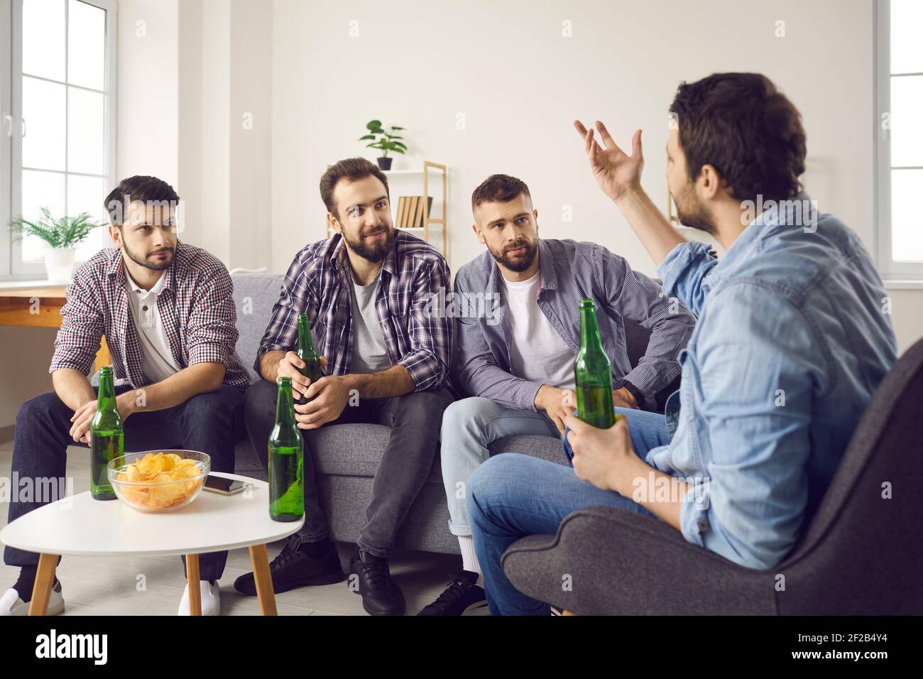 Four positive men friends having home party with beer and chips sitting ...