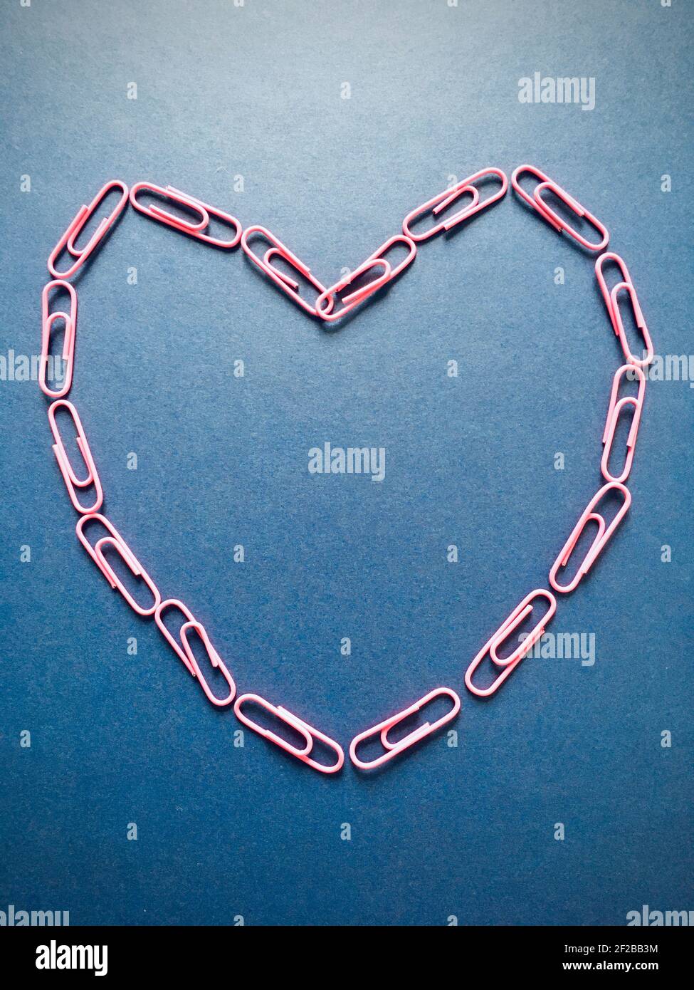 Paper clips arranged in a heart shape on a blue background Stock Photo ...