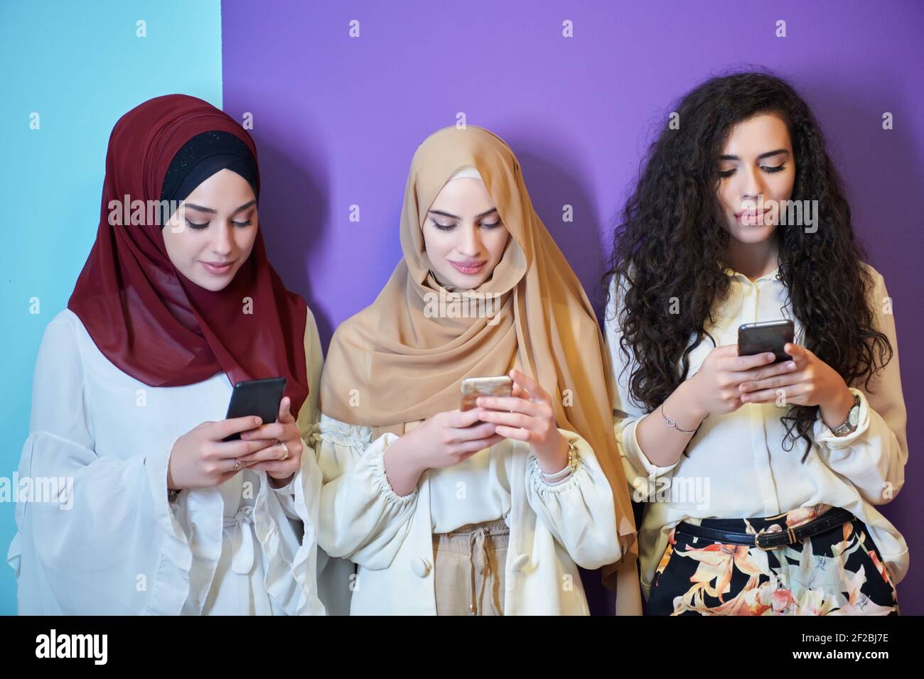 Muslim women using mobile phones isolated on blue and purple background ...
