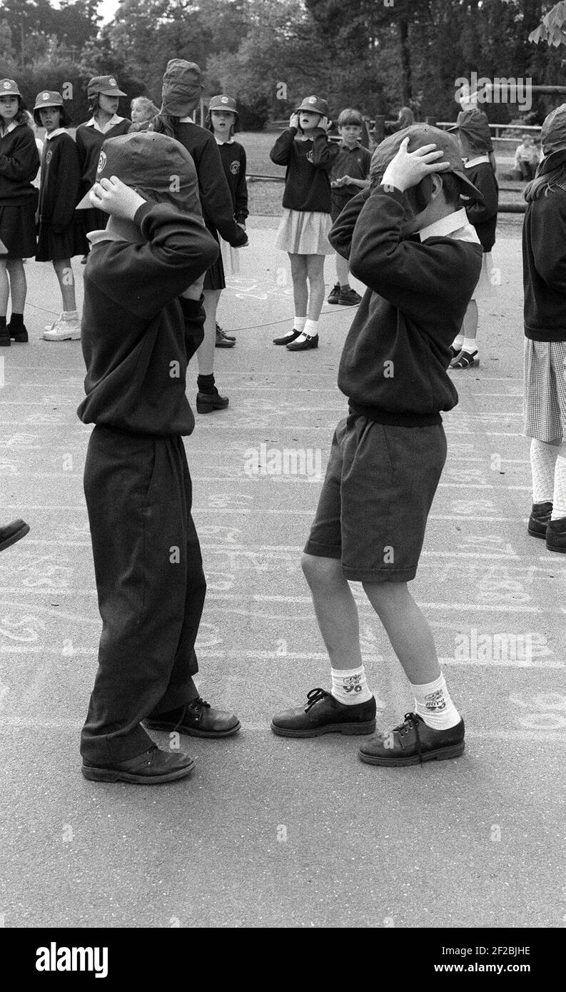 Two young lively schoolboys swap hats in the playground at break ...