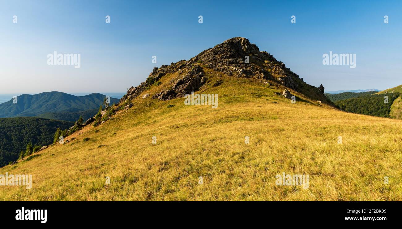 hill covered by meadow with rock formation on summit and other hills on ...