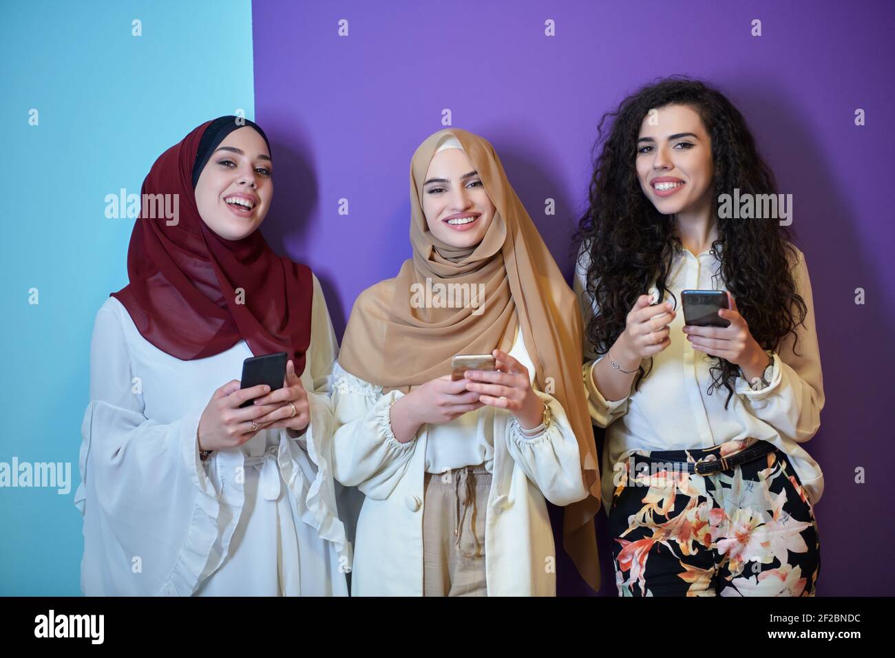 Muslim women using mobile phones isolated on blue and purple background ...