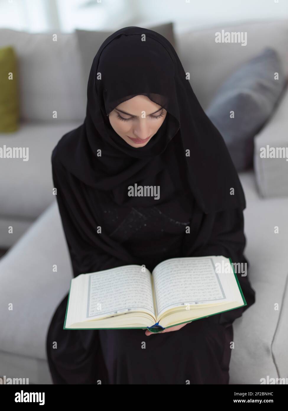 Portrait of young muslim woman reading Quran in modern home. Arabic ...