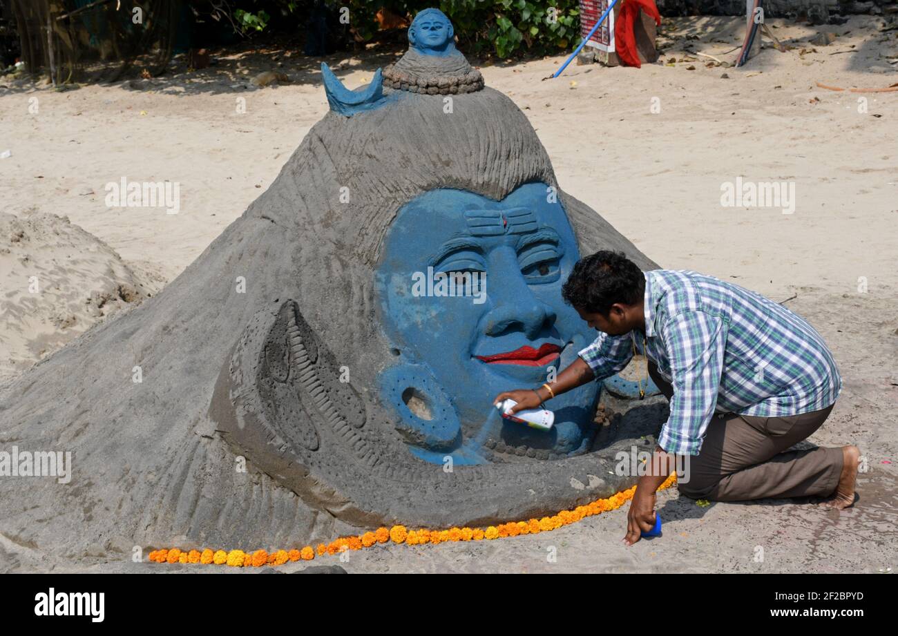 A man sprays colour on the sand sculpture of lord Shiva prepared on the ...