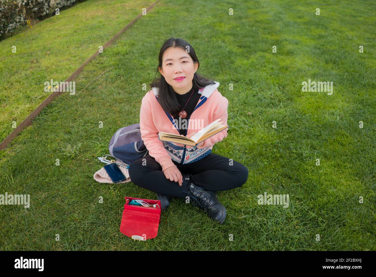 young Asian woman enjoying novel on grass - lifestyle portrait of young ...