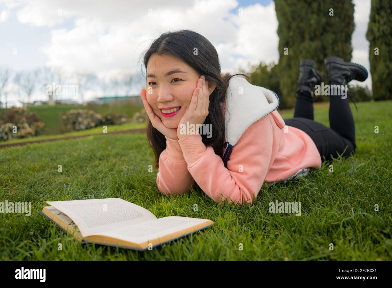 young Asian woman enjoying novel on grass - lifestyle portrait of young ...