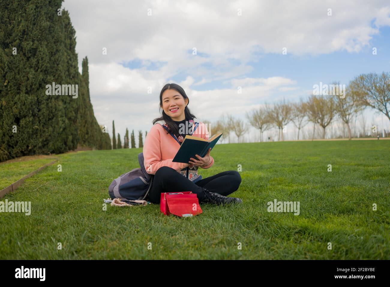 young Asian woman enjoying novel on grass - lifestyle portrait of young ...