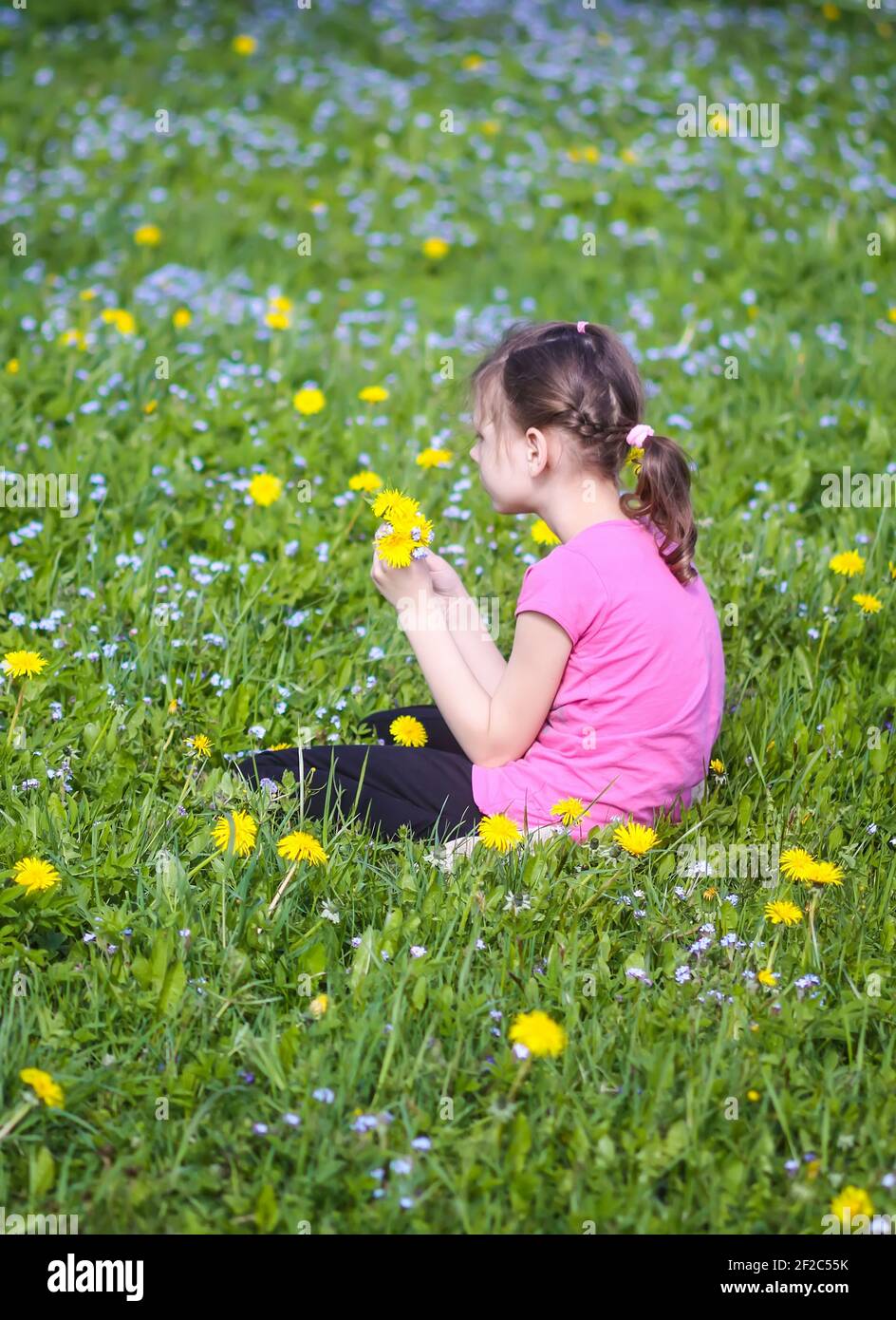 A girl on the green spring meadow with a lot of wildflowers in sunlight ...