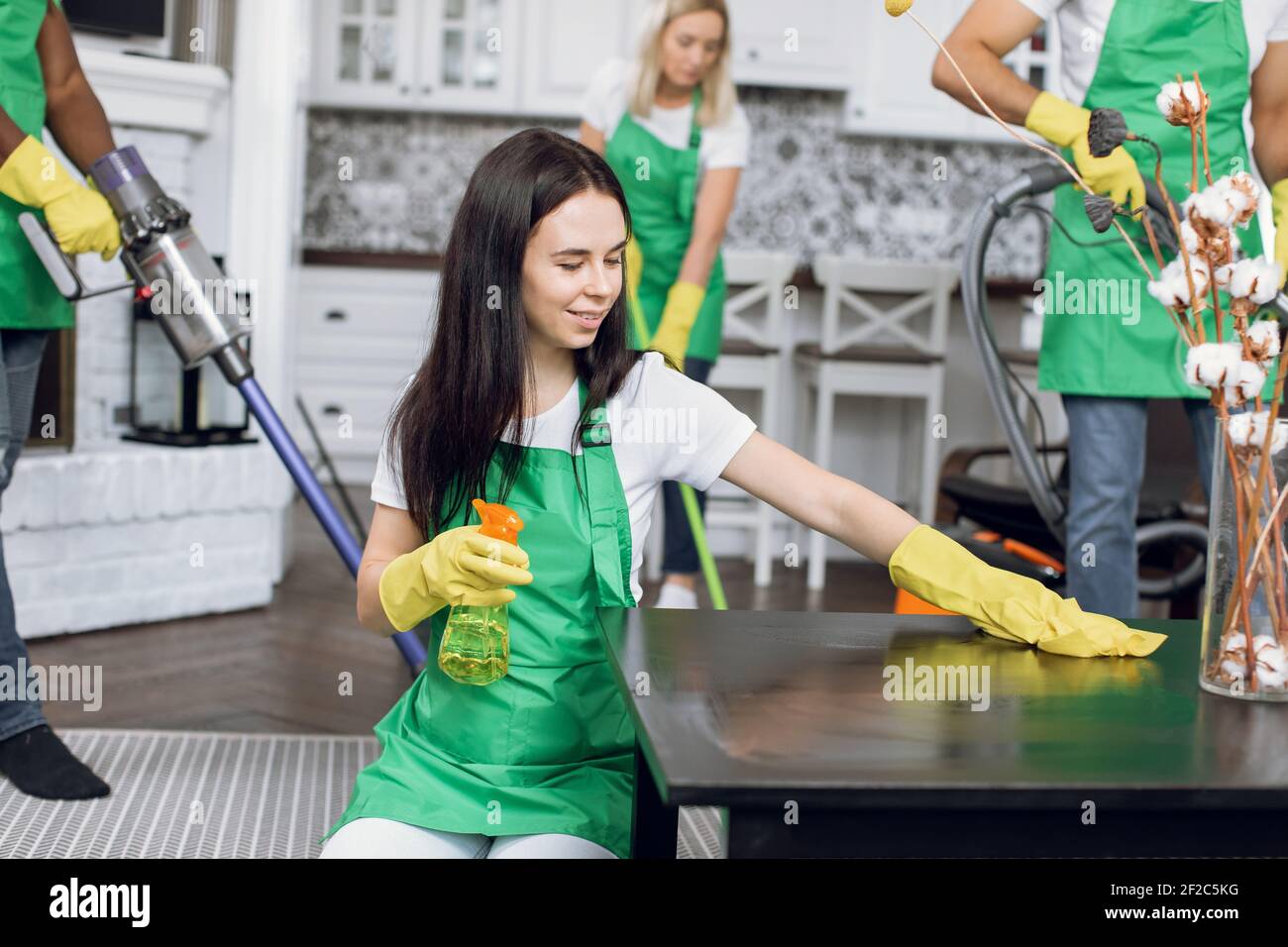 Attractive happy young brunette woman wiping table with microfiber rag ...