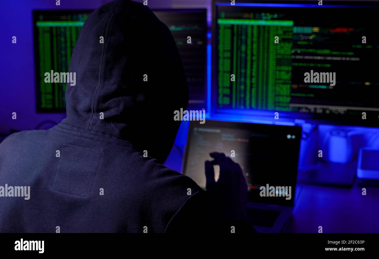 man in a hood working as a hacker at the computer in the dark room at ...