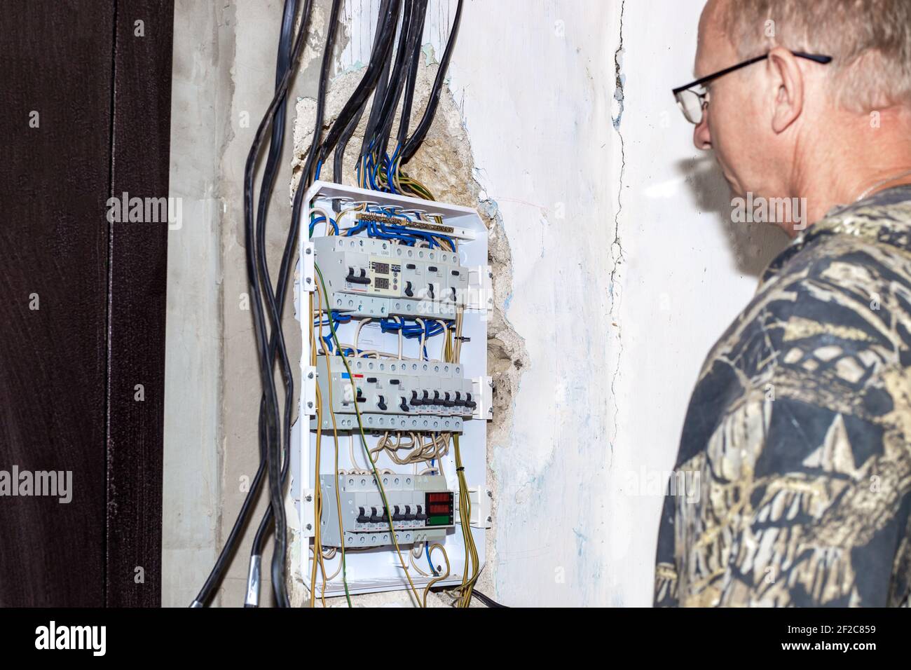 An electrician installs an electrical panel built into the wall of the ...