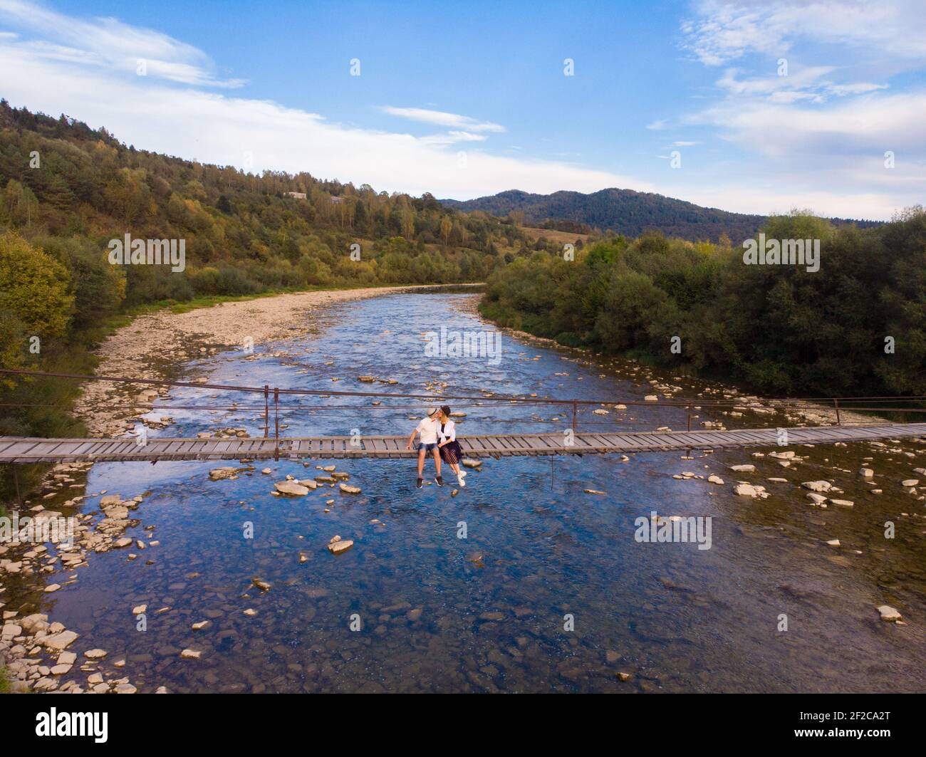 Young traveler couple sits on wooden bridge across mountains river with ...
