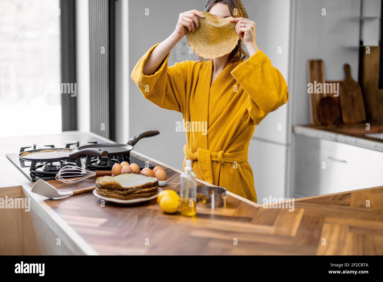 Portrait of a young joyful woman covering her face with fried pancake ...