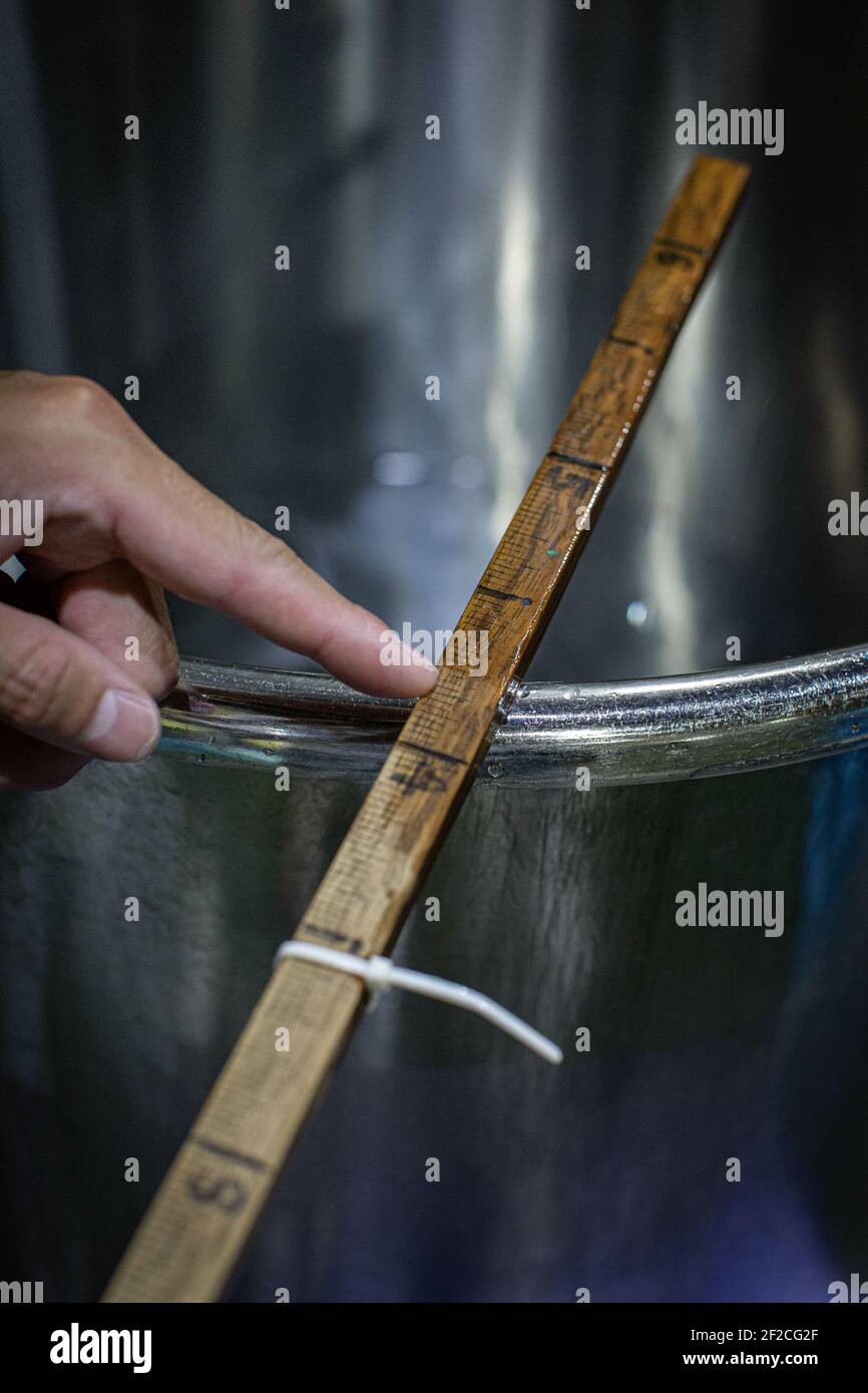 Hand with wooden metre stick diluting the sake with water — to adjust ...