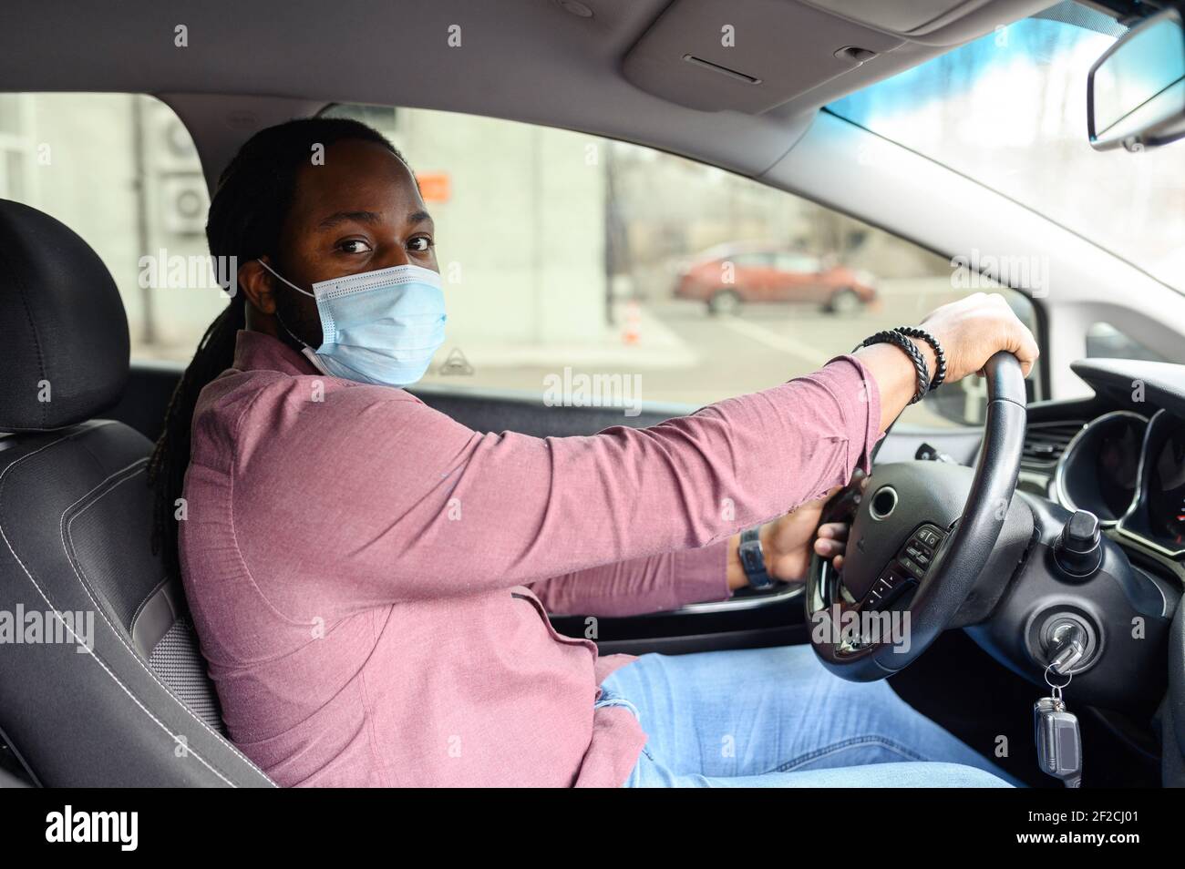 An African-American man wearing medical mask driving a car, a taxi ...