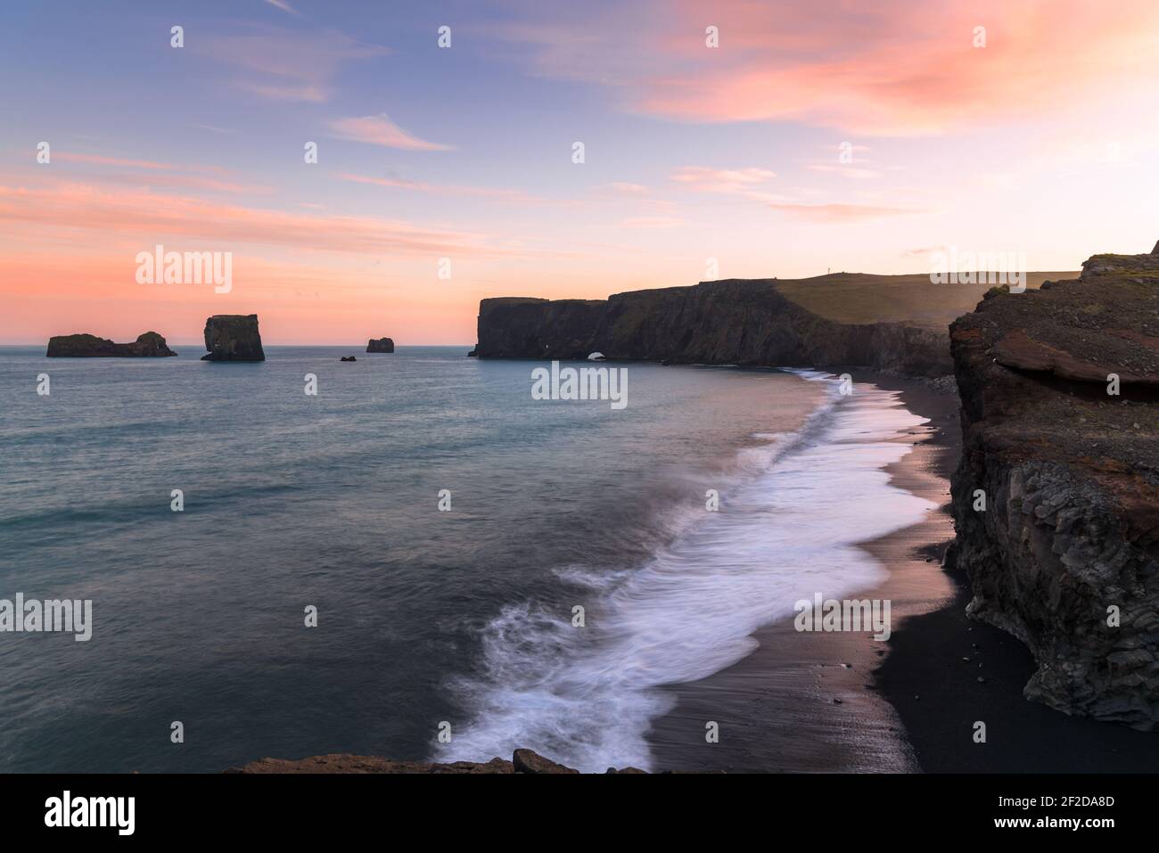 Rocky promontory overlooking a bay and a black sand beach under a ...