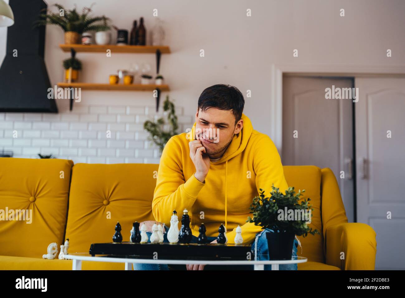 Young man sitting on yellow sofa and playing chess in room. Male ...