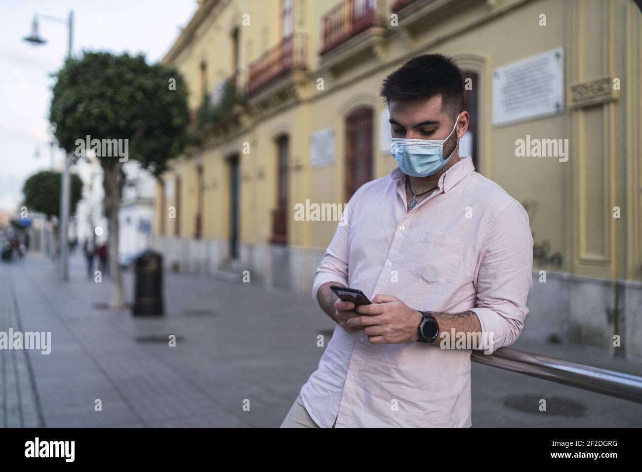 A handsome Spanish man wearing a mask and typing on his phone - new ...