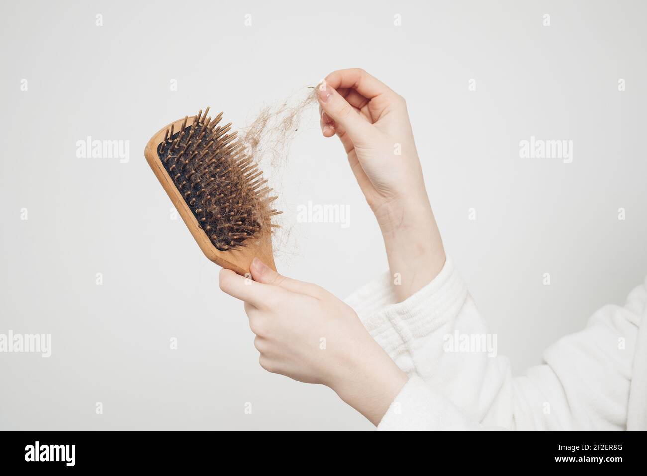 woman removes a bun of hair with a wooden comb on a light background ...