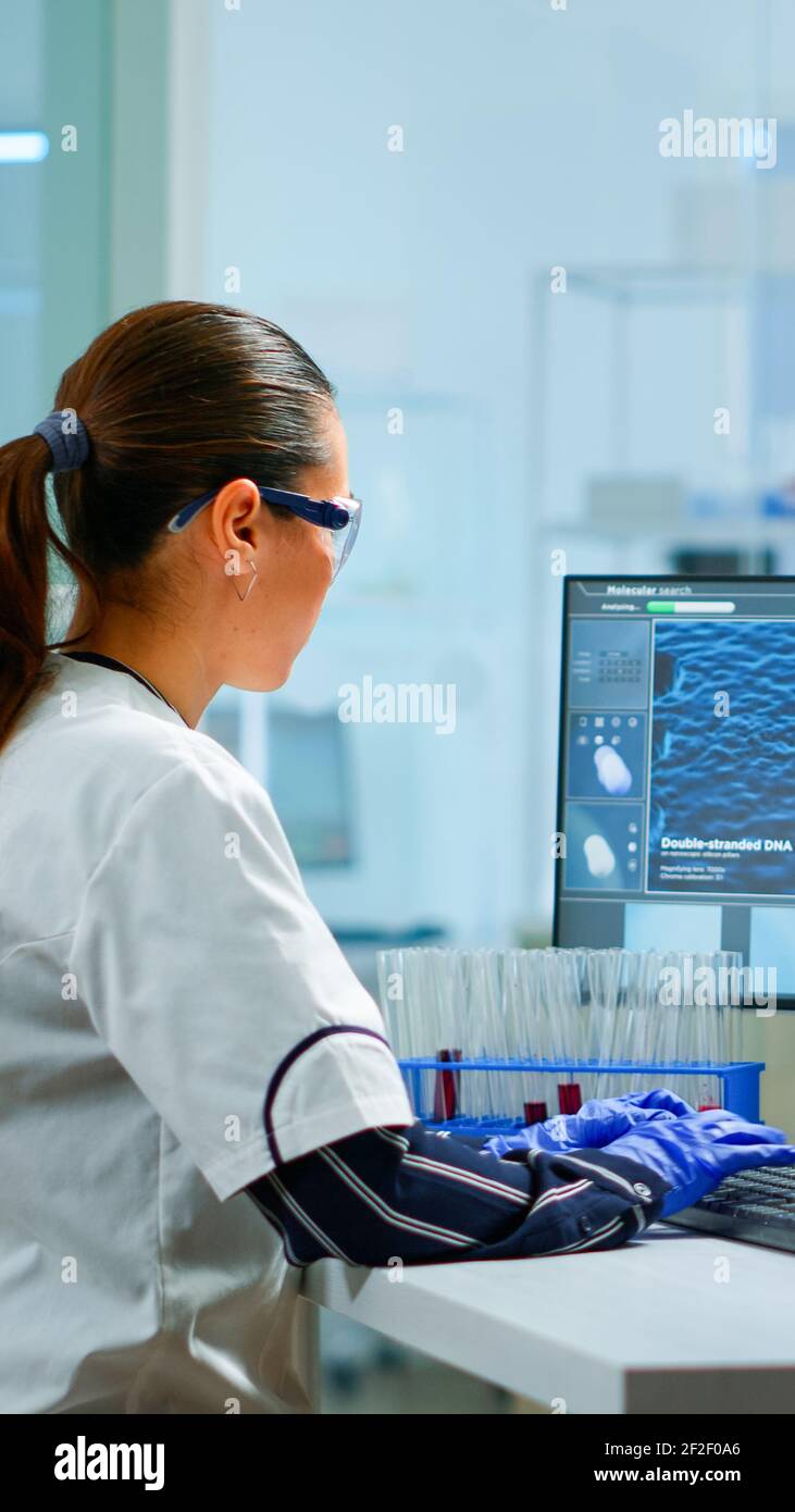 Chemistry doctor analysing blood sample and typing on computer while ...