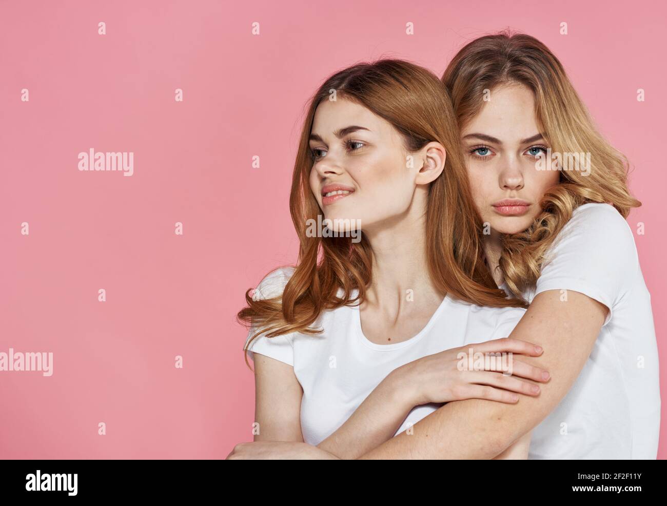 Two glamorous girlfriends hugs caring emotions fun pink background ...