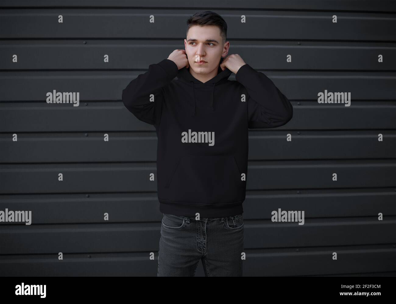 Mockup of a black hoodie with a pocket on a guy, straightening a hood ...