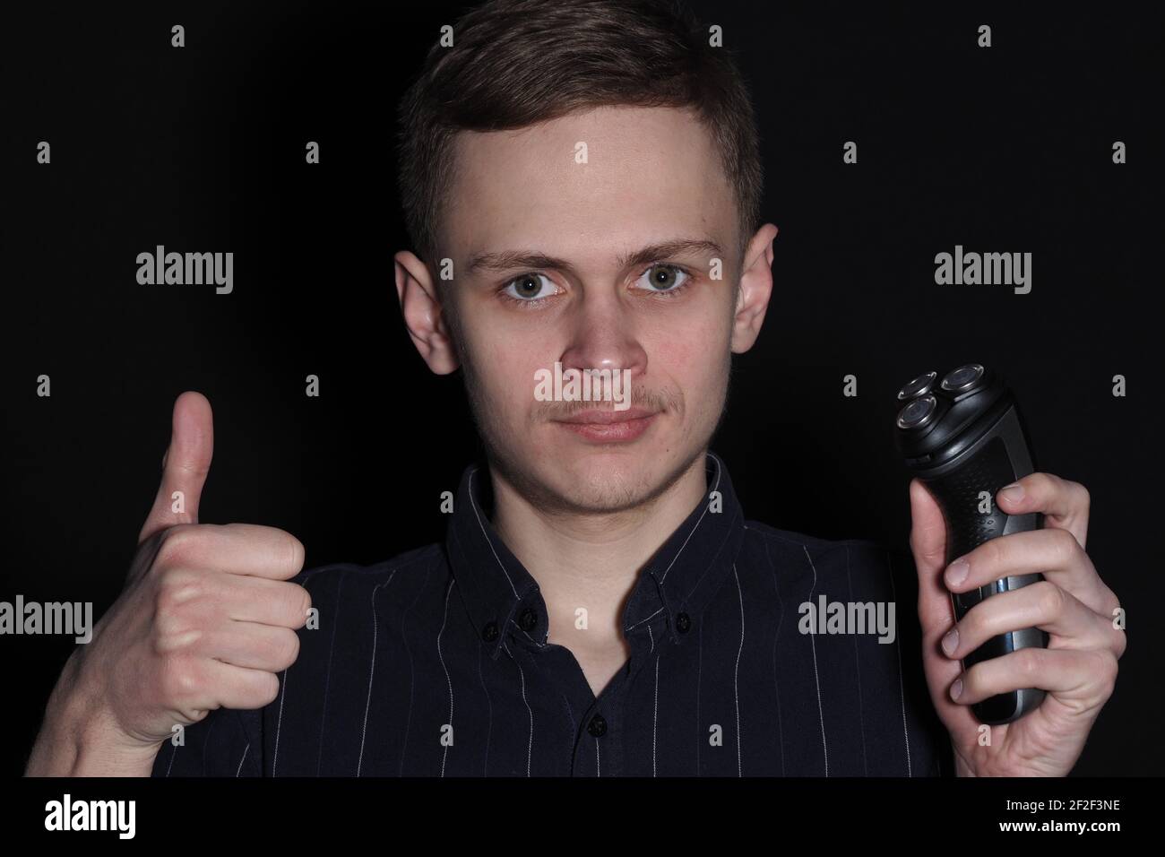 Portrait of a young man of European appearance with an electric razor ...