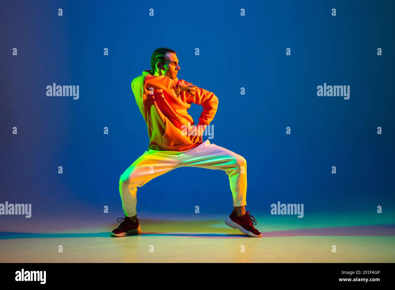 Young hip-hop dancer dancing isolated over on blue background in neon ...