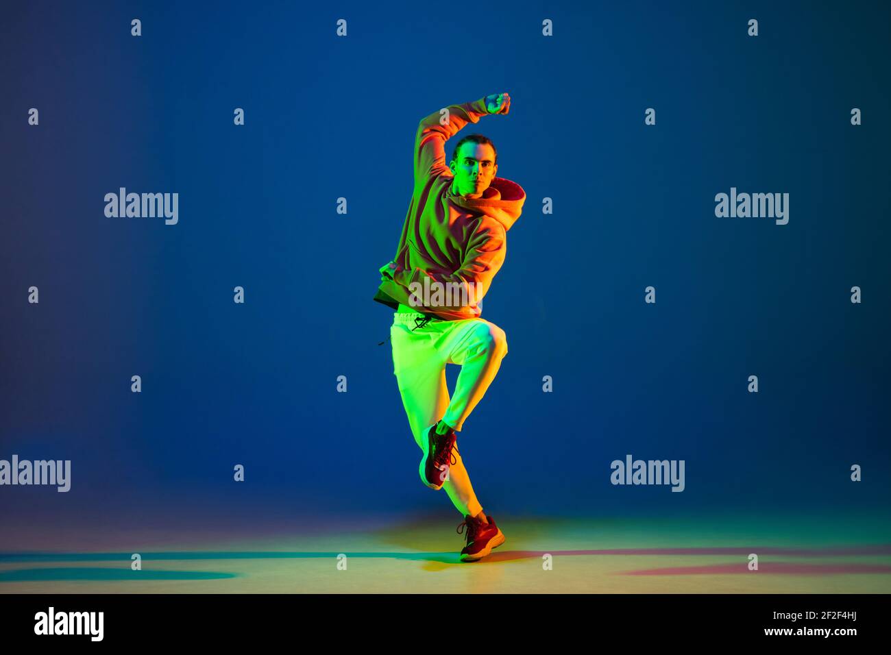 Young man dancing hip-hop in stylish attire on blue background in neon ...