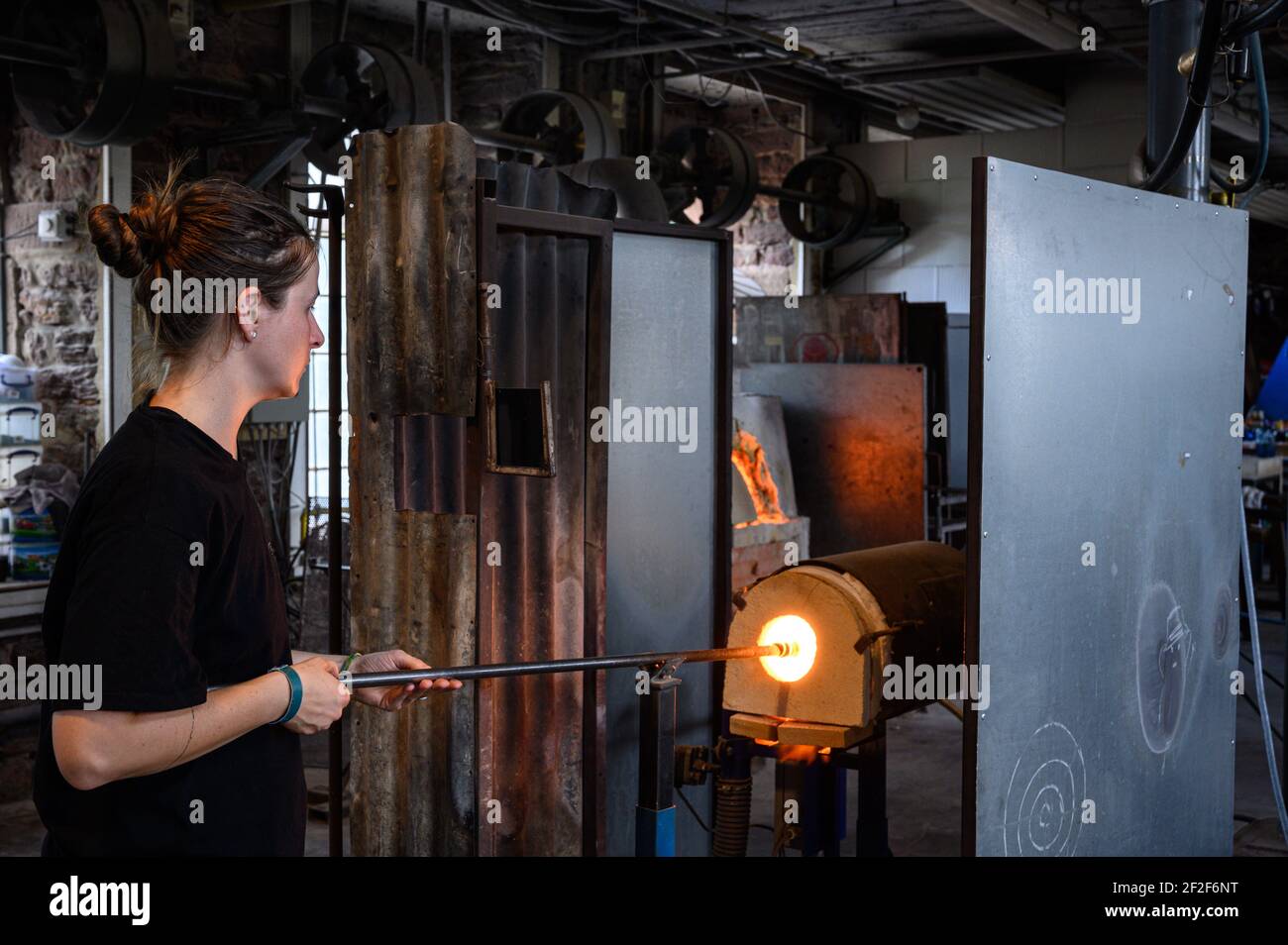 Adult female worker melting glass in furnace. Holding and Turning with ...