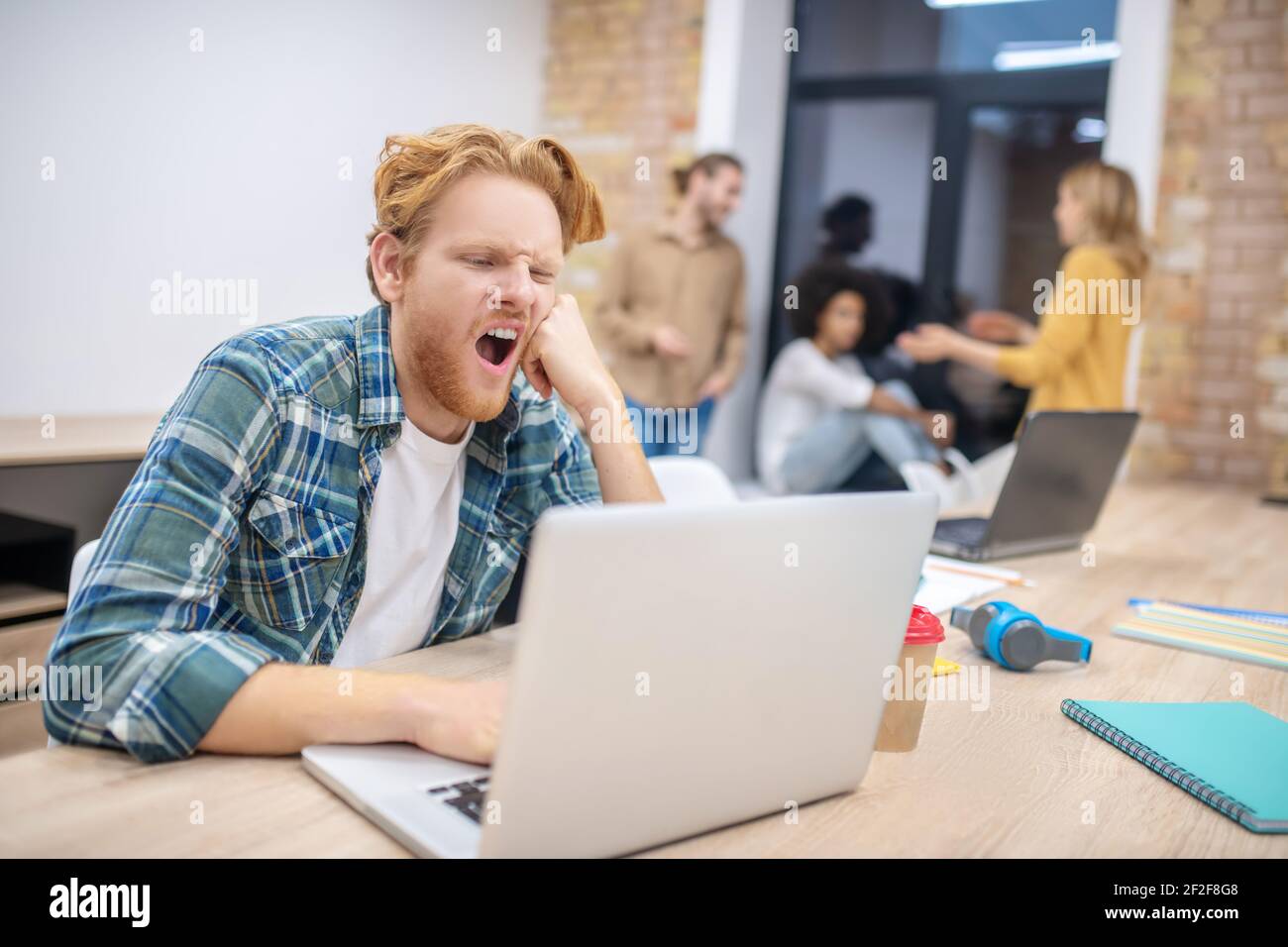 Ginger guy working on a laptop and yawning Stock Photo - Alamy